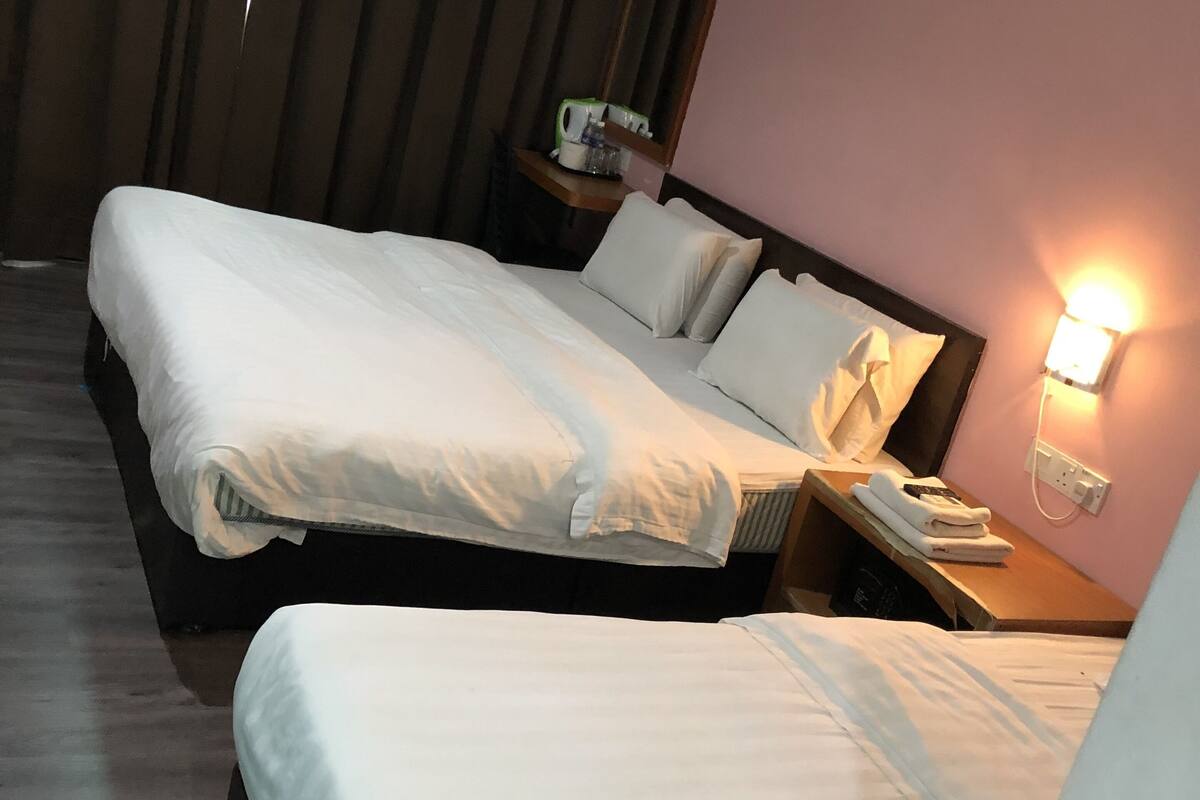 Quarto de hotel com duas camas, uma mesa de cabeceira com abajur e um ar condicionado na parede.