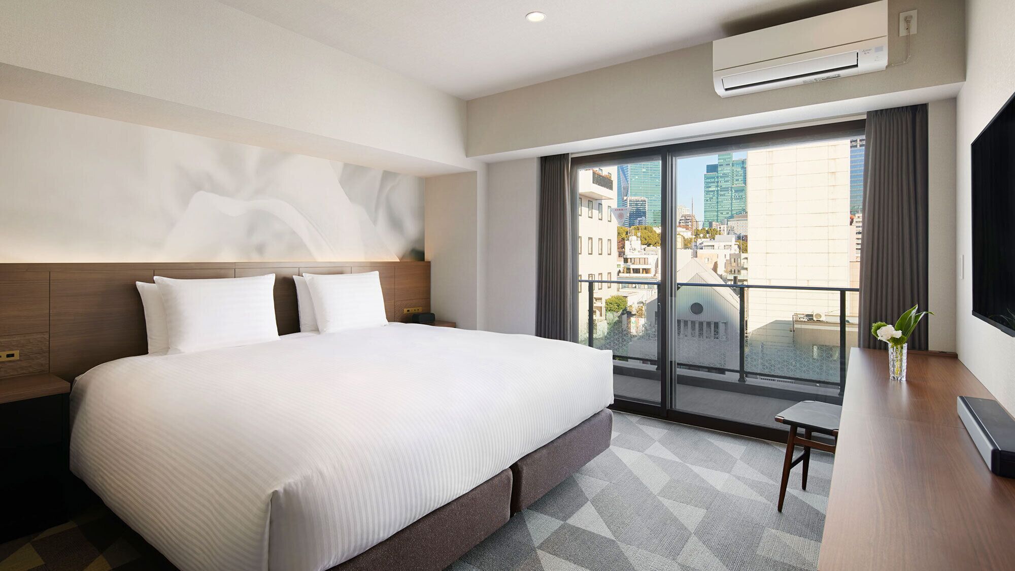 Quarto de hotel com uma cama grande, uma escrivaninha, uma cadeira, televisão e varanda com vista para a cidade.
