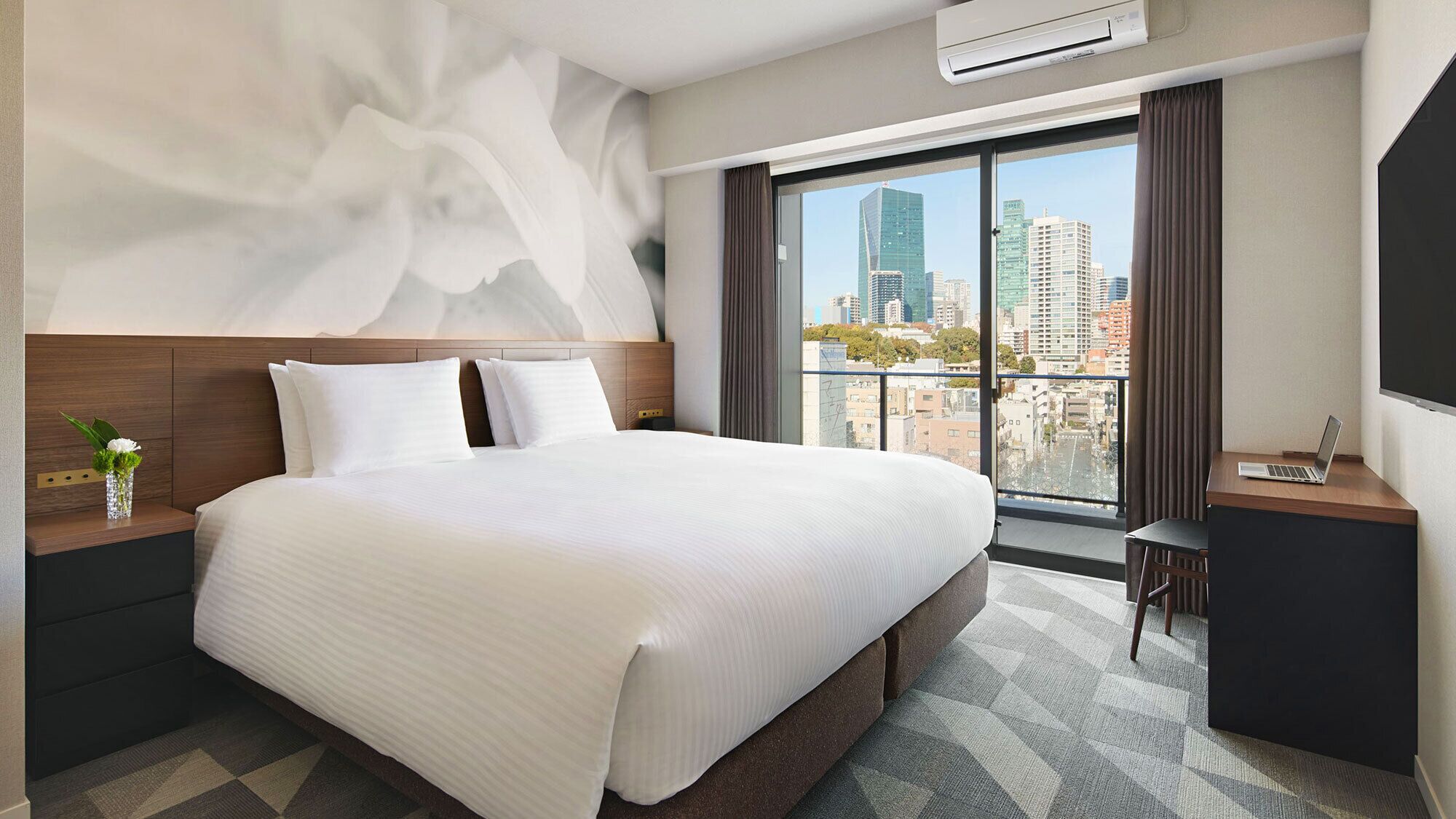 Quarto de hotel moderno com cama grande, escrivaninha e vista para a paisagem urbana.