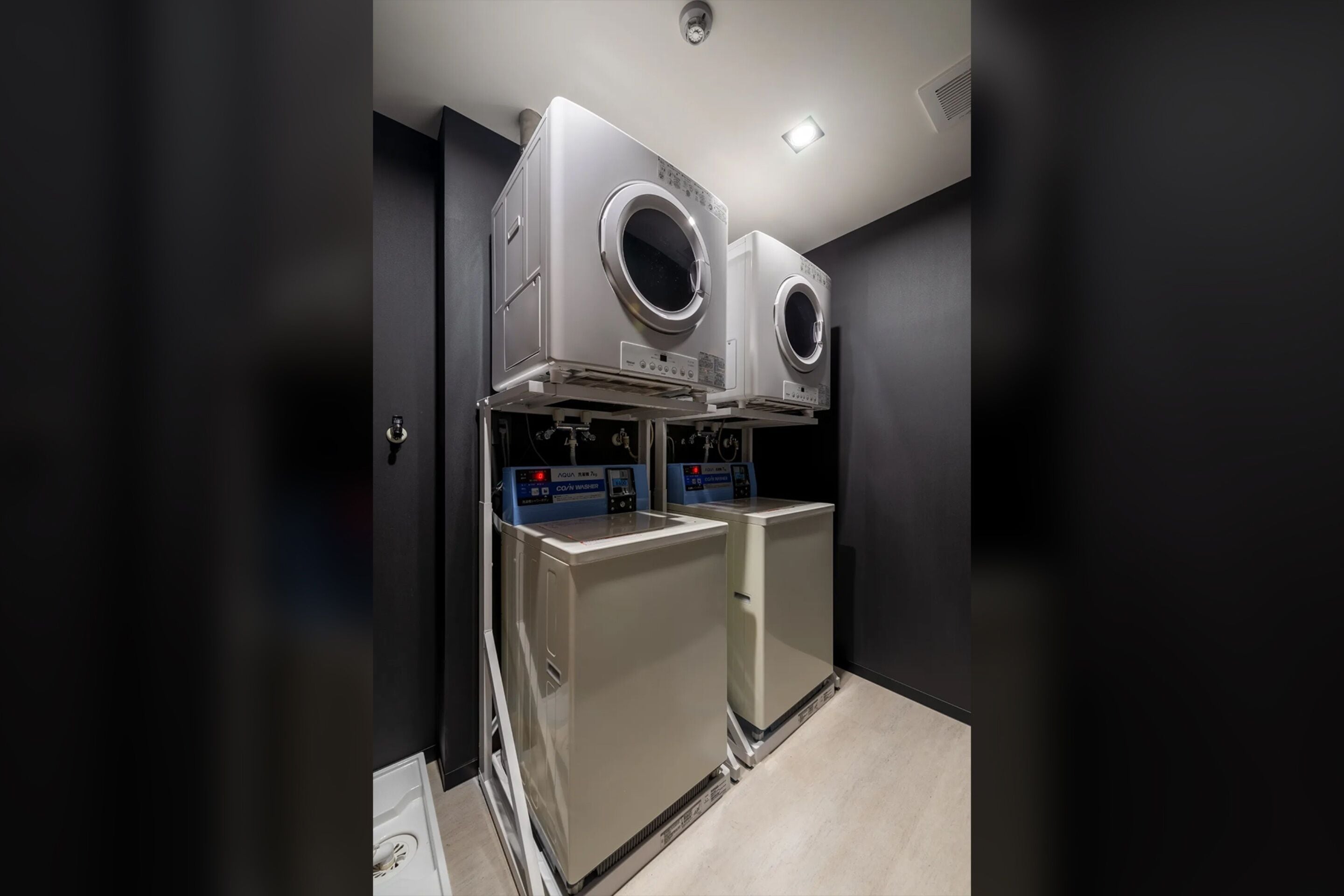 Uma lavanderia moderna com duas máquinas de lavar e secar empilhadas, um painel de controle e uma ventilação no teto.