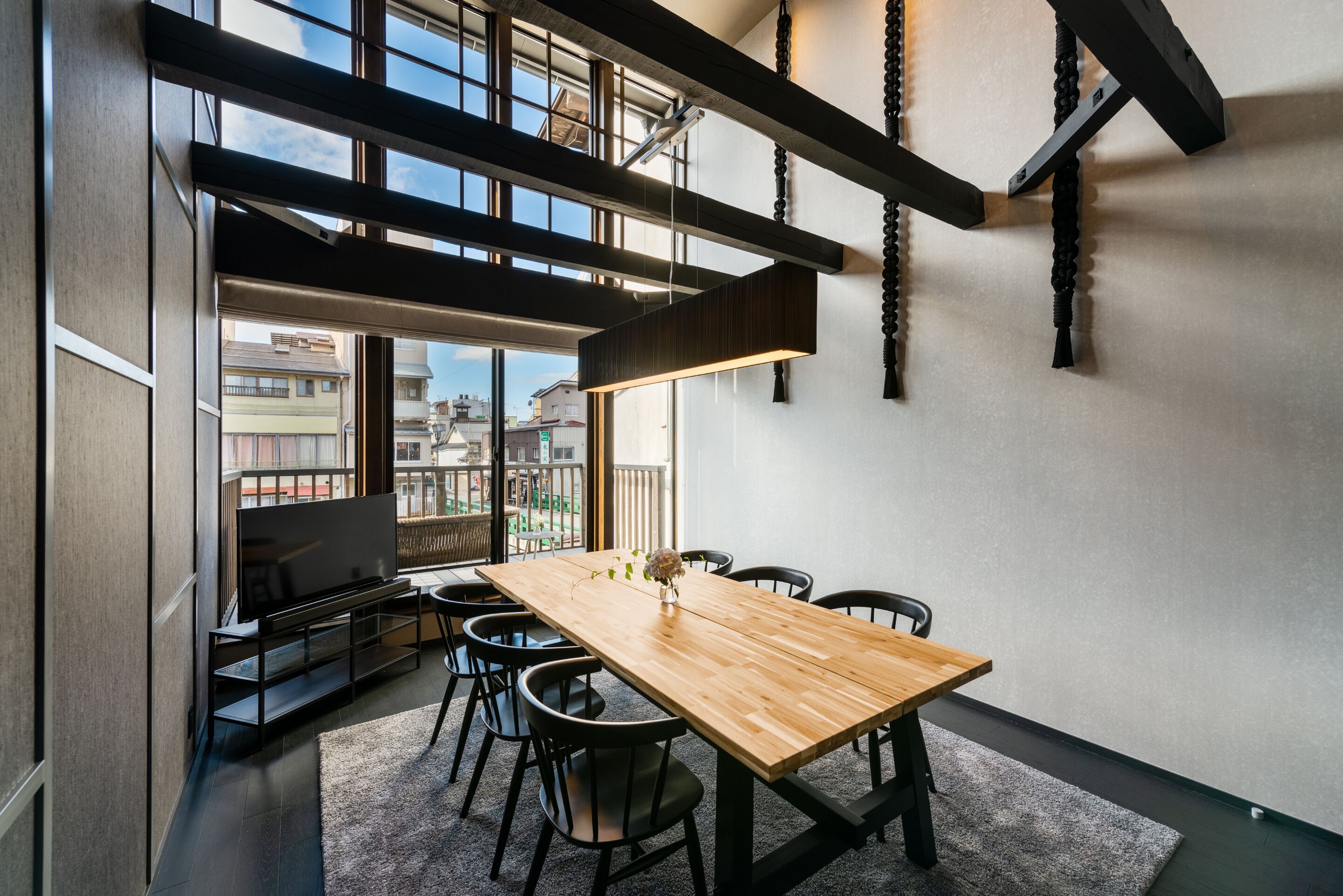 Uma sala de jantar moderna com uma mesa de madeira, cadeiras pretas e uma televisão sobre um suporte.