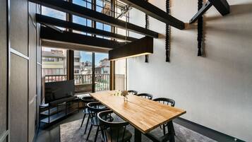 Uma sala de jantar moderna com uma mesa de madeira, cadeiras pretas e uma televisão sobre um suporte.