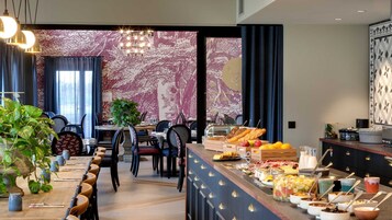 Uma área de jantar moderna com uma mesa comunitária grande, cadeiras e um buffet com diversos alimentos.