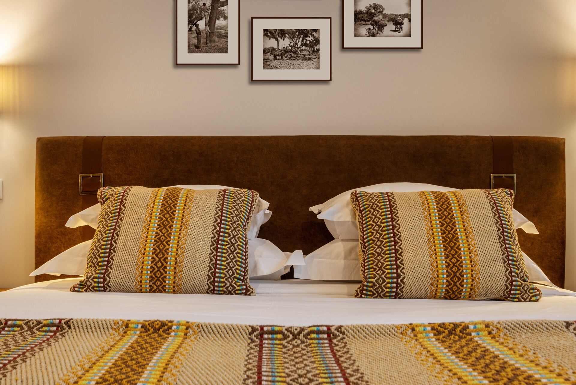Uma cama com almofadas estampadas e um cobertor coordenado, com fotografias em preto e branco na parede.