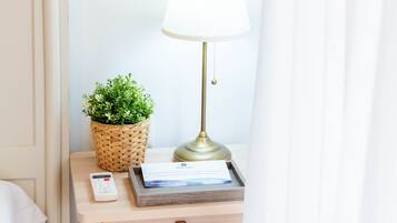 Uma mesa de cabeceira de madeira com abajur, uma pequena planta em vaso e um cartão.