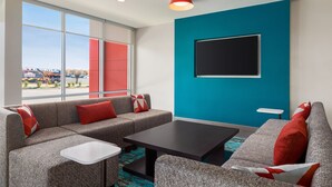 Uma sala de estar moderna com um sofá seccional, uma mesa de centro e uma TV de tela plana fixada em uma parede verde-água. Grandes janelas oferecem vista para o exterior.