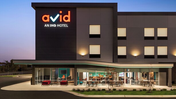 Um hotel moderno com um letreiro 'avid' bem visível, entrada de vidro e área externa com mesas e cadeiras.