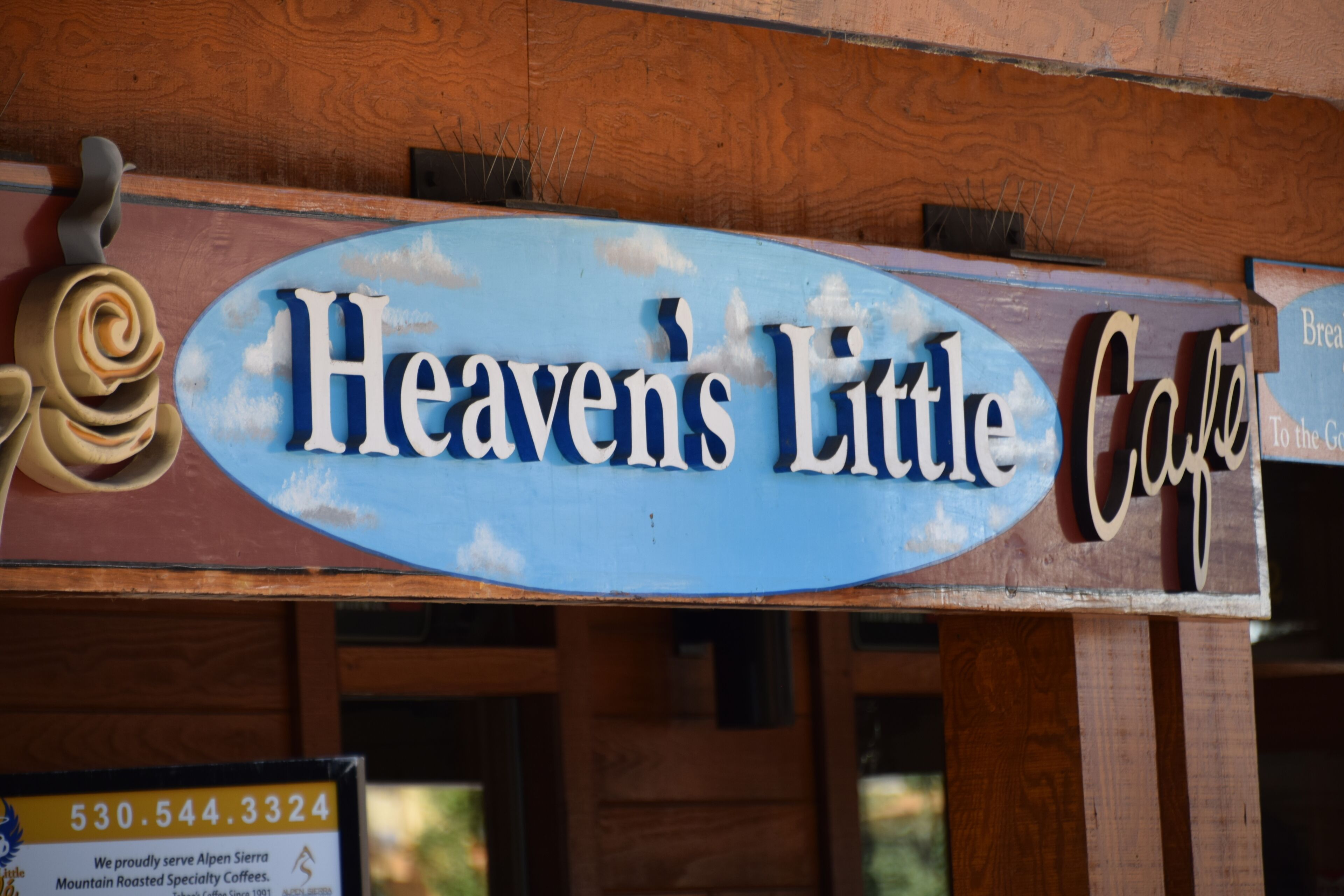 Uma placa de madeira com o texto 'Heavens Little Cafe' e um número de telefone.