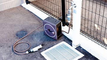 Uma caixa de serviços, uma grade de metal e uma mangueira em uma superfície de concreto perto de uma cerca.