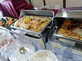 Uma mesa de buffet com diversos pratos, incluindo arroz e um item assado, e um prato de frutas.