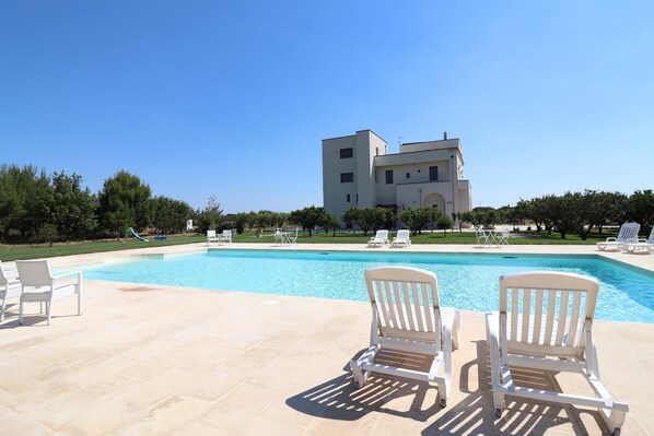 Piscina com espreguiçadeiras e um edifício ao fundo.