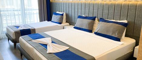 Quarto de hotel com duas camas, cada uma com colcha azul e branca, e cabeceira estofada cinza.