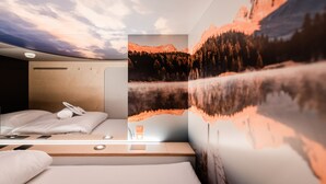 Quarto com cama, mesa de cabeceira e um mural na parede com paisagem de montanhas.