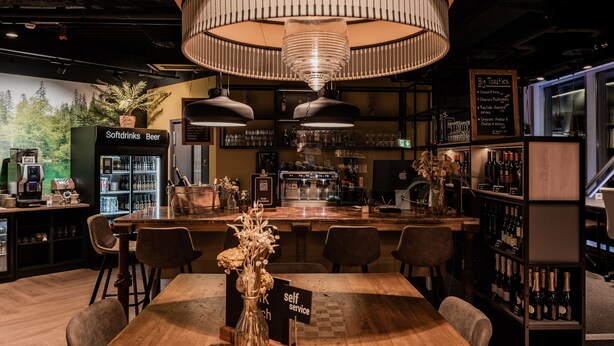 Uma área de bar com balcão de madeira, vários bancos altos, uma máquina de café e um resfriador de vinhos.