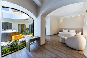 Quarto de hotel moderno com teto curvo, área de estar com uma mesa pequena, uma cama grande e vista para a área externa.