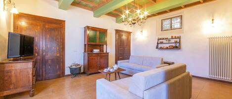 Uma sala de estar com sofá, televisão, armários de madeira e um candelabro.