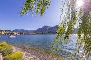 Um lago com vista clara para montanhas ao fundo, um caminho de pedra ao longo da margem e vegetação em primeiro plano.