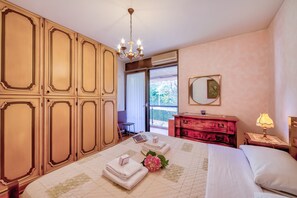 Quarto de hotel com cama grande, guarda-roupa, penteadeira, espelho e janela com vista para o verde.