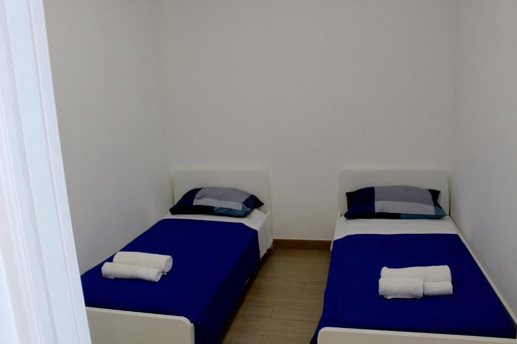 Um quarto pequeno e estreito com duas camas de solteiro, cada uma com colcha azul e travesseiros brancos.