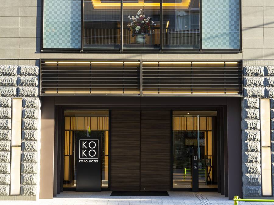 Uma entrada de hotel moderna com um logotipo destacado, grandes portas de vidro e fachada bem iluminada.