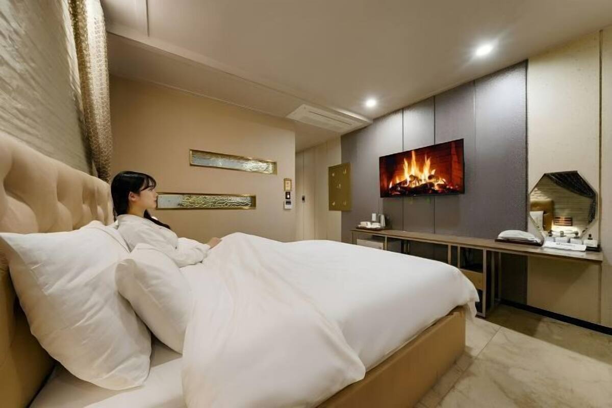 Quarto de hotel com uma cama grande, uma TV fixada na parede e uma escrivaninha com abajur.