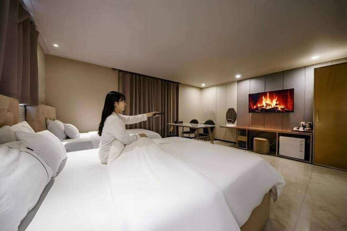 Quarto de hotel moderno com uma cama grande, uma escrivaninha, uma cadeira e uma televisão de tela plana na parede.