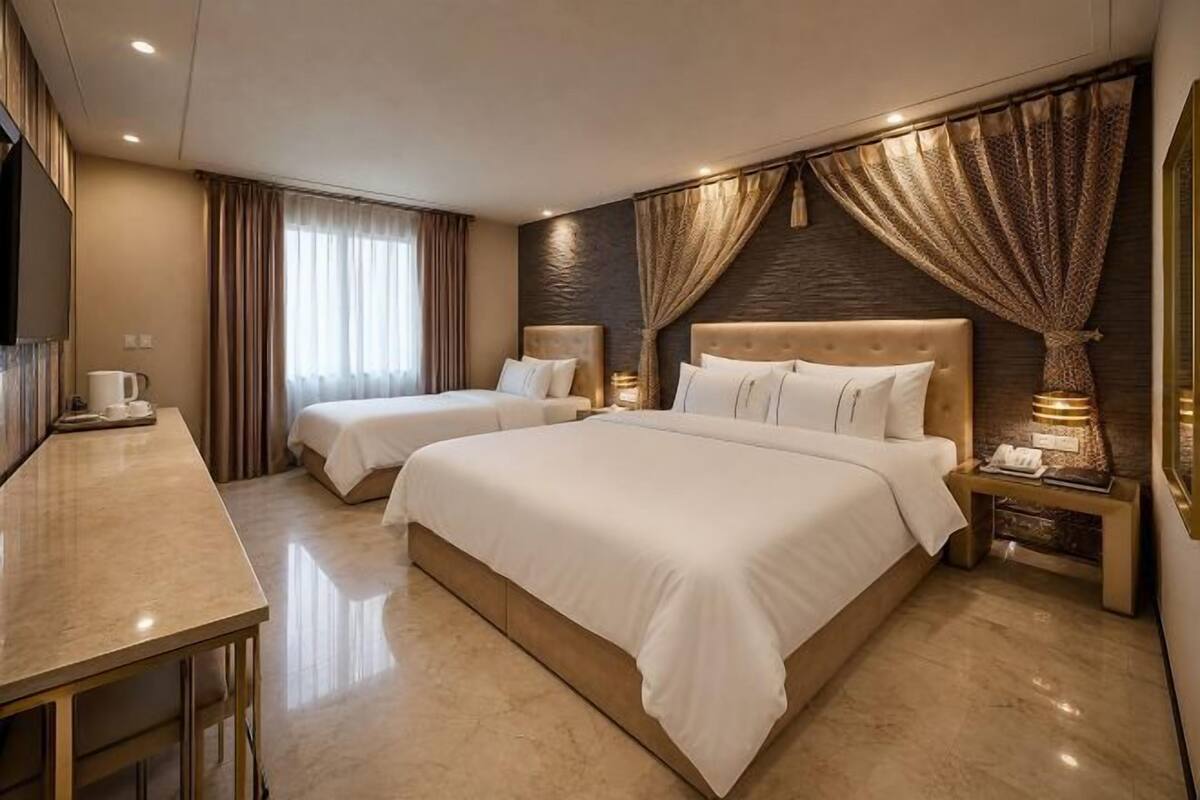 Quarto de hotel com duas camas, uma escrivaninha, televisão de tela plana e uma janela grande com cortinas.