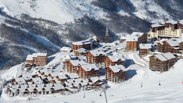 Uma estância de esqui coberta de neve, com vários edifícios de chalés, pistas de esqui e um teleférico.