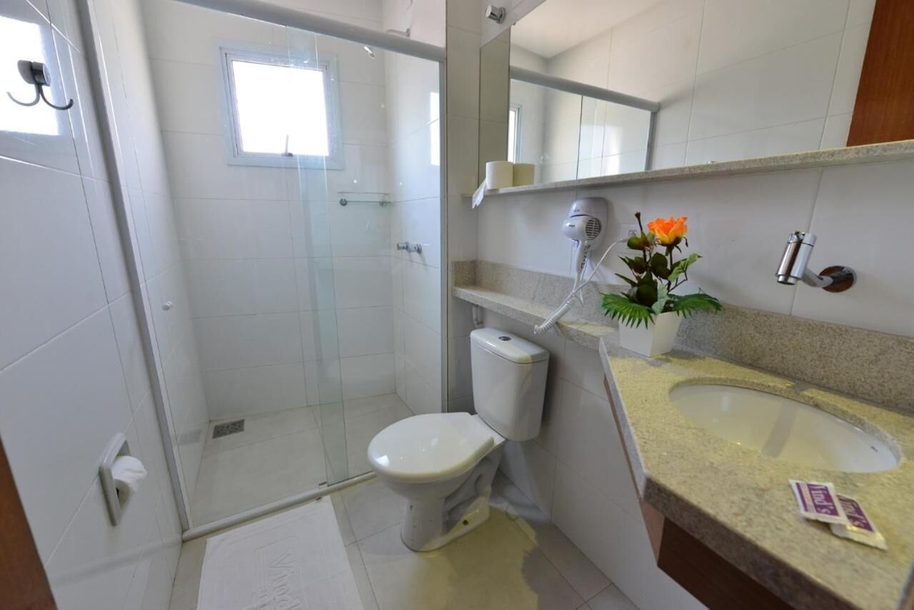 Uma casa de banho com cabine de duche em vidro, sanita, lavatório com bancada de granito e espelho sobre o lavatório.