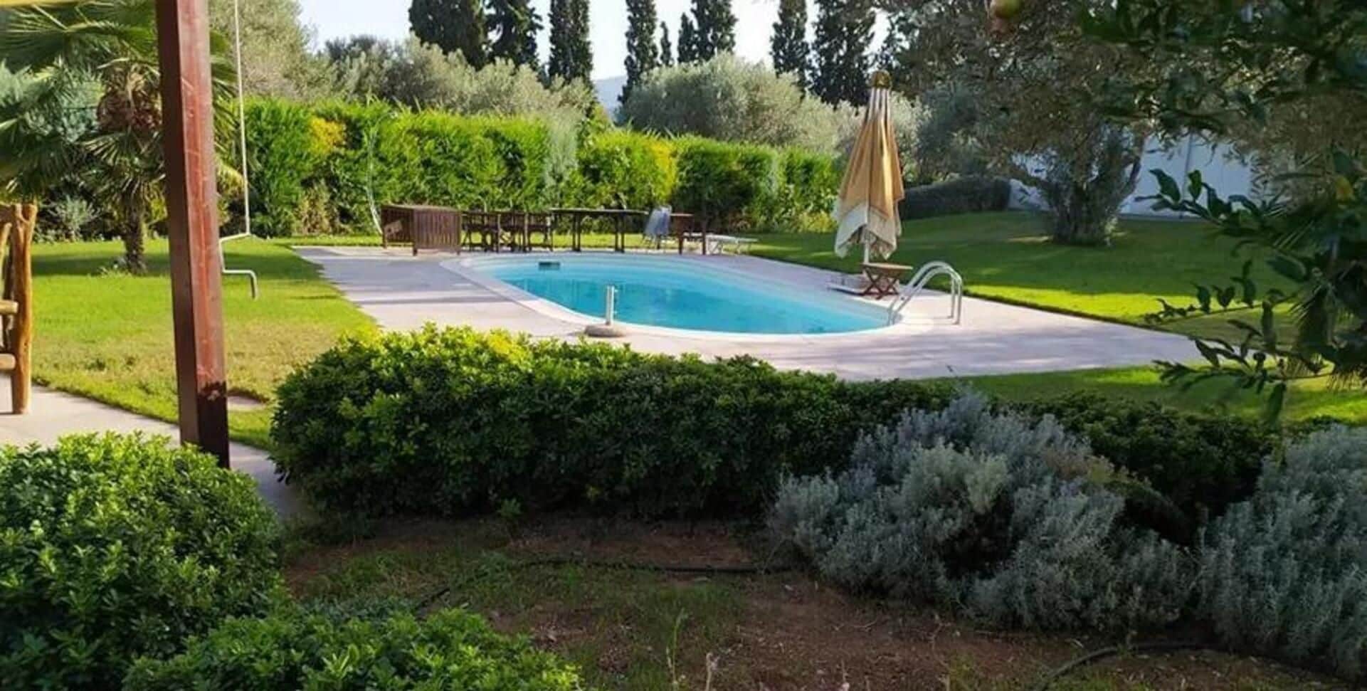 Piscina rodeada por sebes bem cuidadas e um gramado.