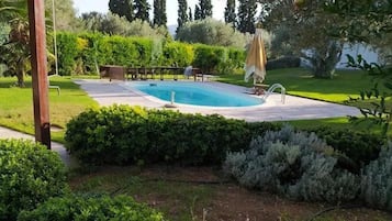 Piscina rodeada por sebes bem cuidadas e um gramado.