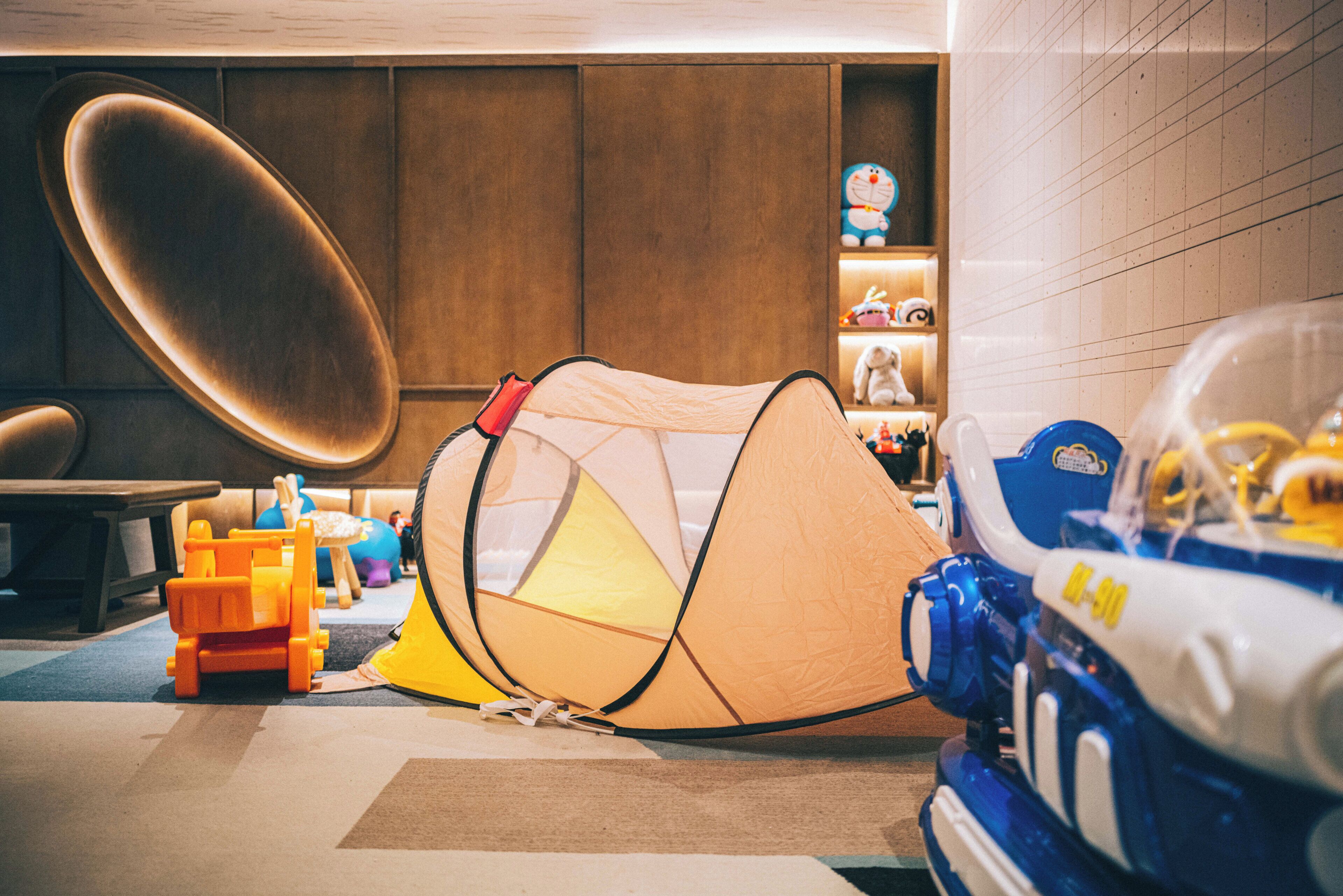 Um quarto com uma estrutura semelhante a uma tenda, um brinquedo azul e branco, e uma estante com diversos objetos.