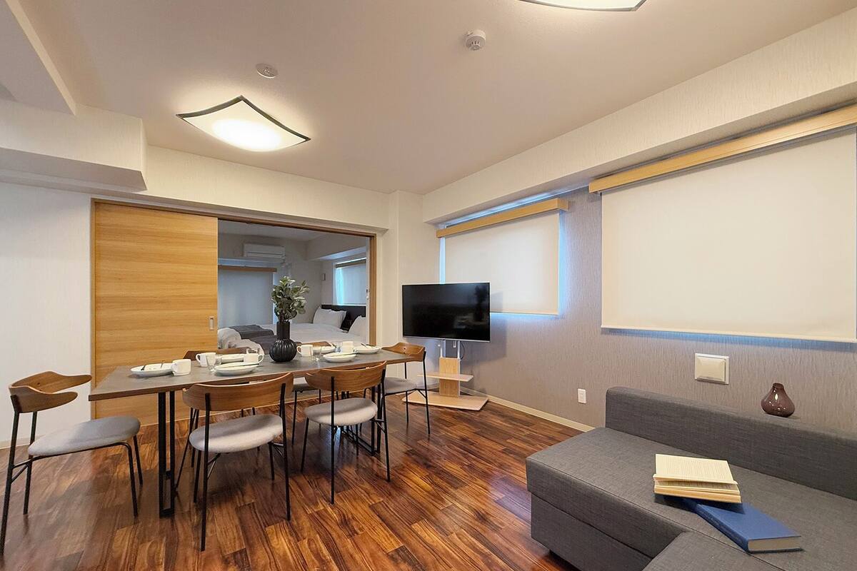 Quarto de hotel moderno com área de refeições, televisão de tela plana, sofá e estante.