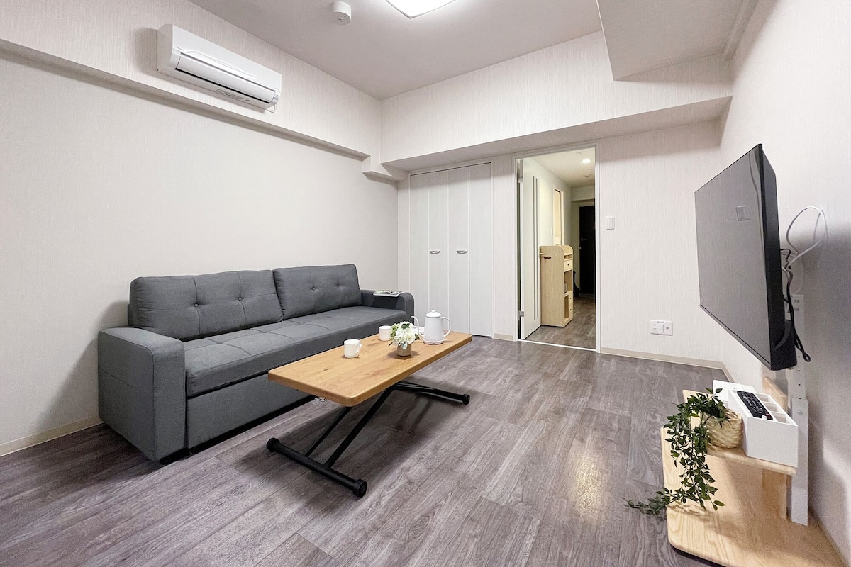 Uma sala de estar moderna com um sofá cinzento, uma mesa de centro de madeira e uma televisão de tela plana presa à parede.