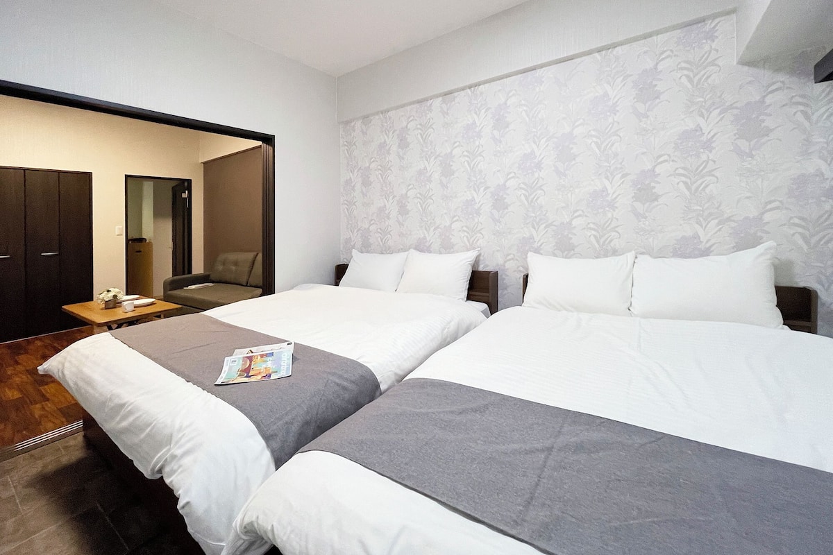 Quarto de hotel com duas camas, piso de madeira, espelho e papel de parede estampado.