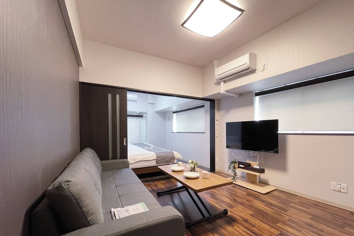 Um espaço de estar compacto com sofá, mesa pequena, TV de tela plana e ar-condicionado.