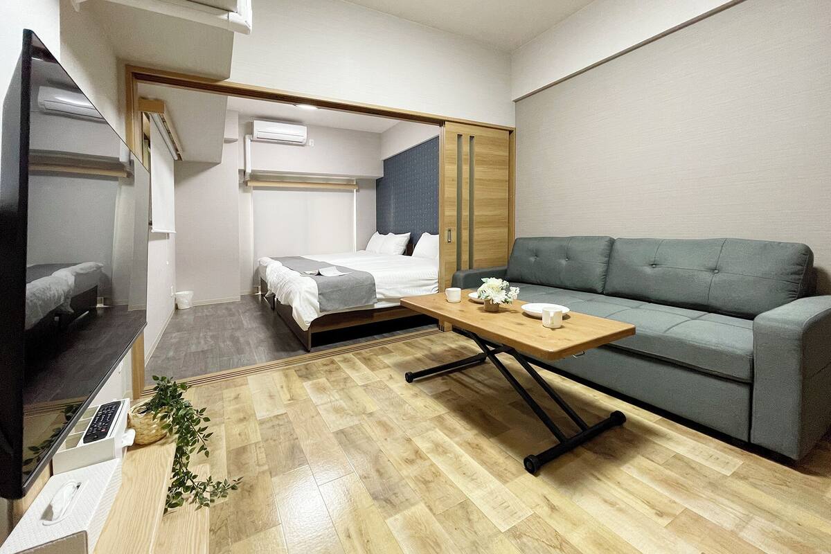 Quarto de hotel compacto com cama, sofá, mesa pequena e escrivaninha com computador.