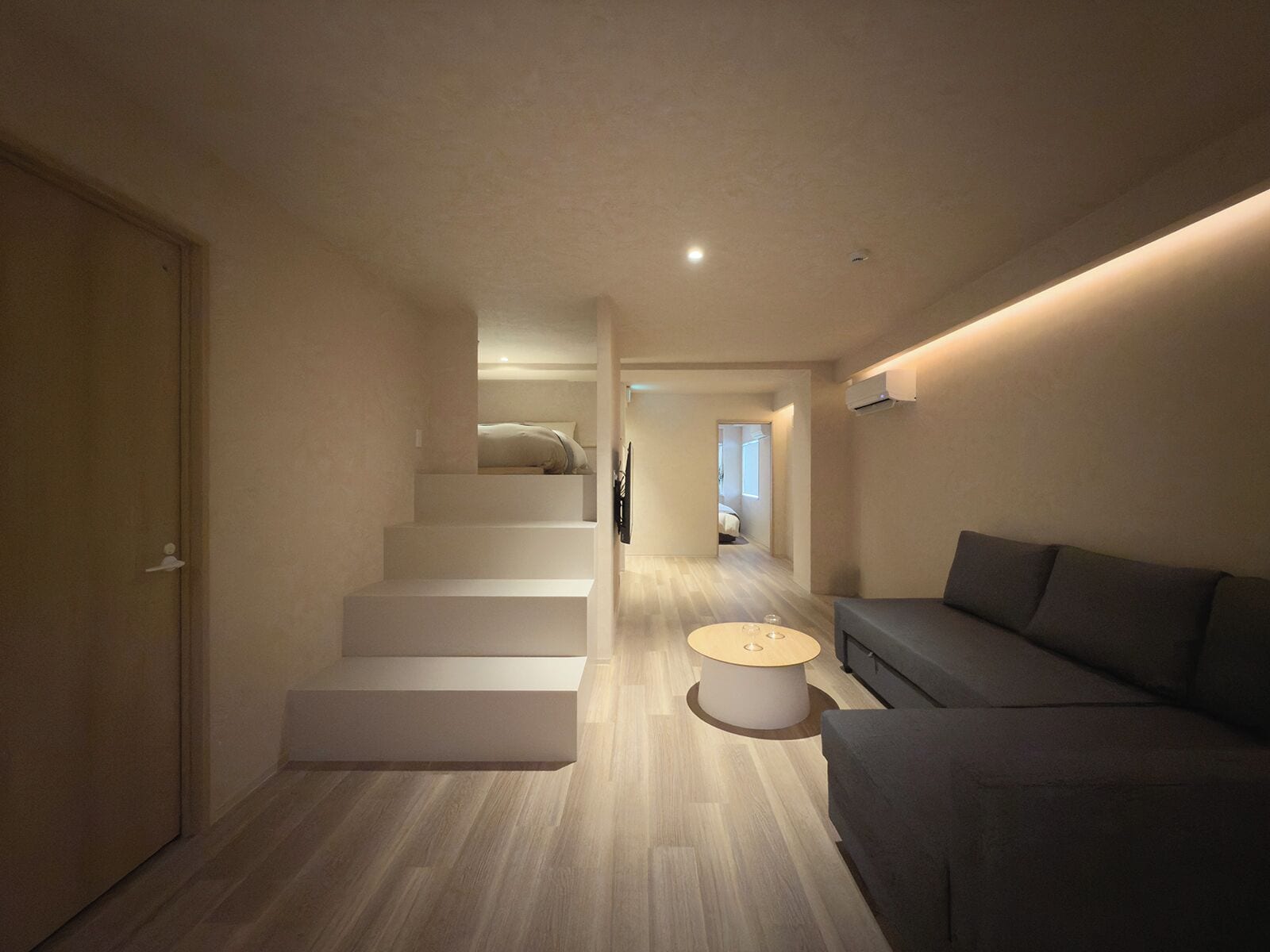 Um interior moderno com uma escada que leva a um quarto, um sofá cinzento e uma mesa de centro redonda.