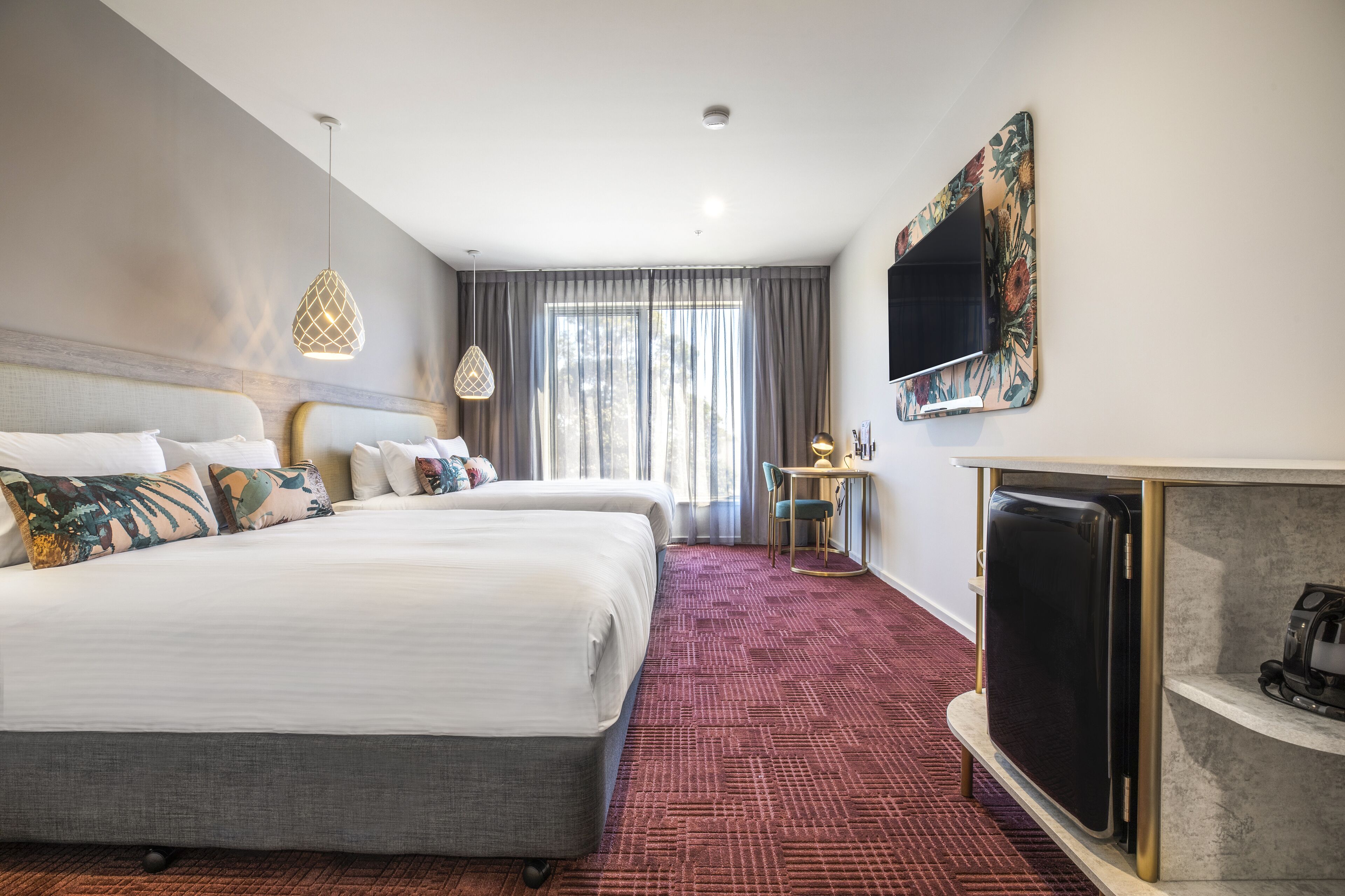 Quarto de hotel com duas camas, televisão, lareira e uma grande janela com cortinas.