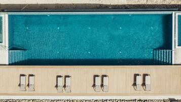Uma piscina retangular com água azul cristalina, rodeada por um deck de madeira com espreguiçadeiras.