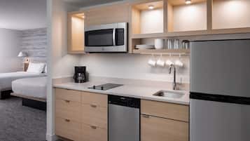 Cozinha moderna equipada com micro-ondas, máquina de lavar louça e frigorífico. Pequena bancada com cafeteira e pia.