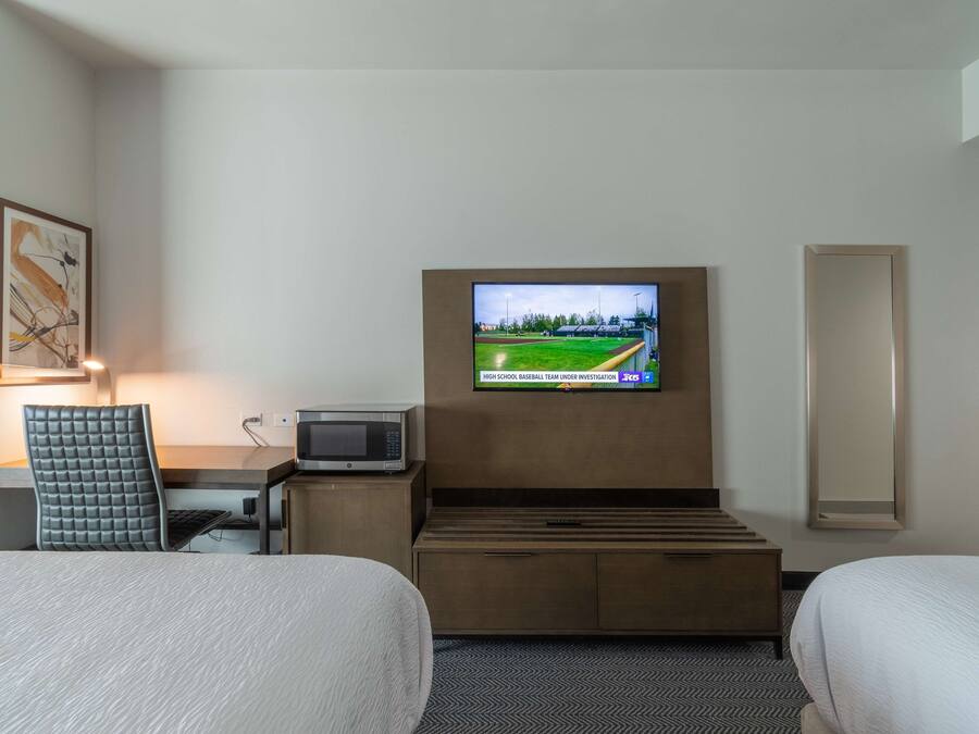 Quarto de hotel com duas camas, uma escrivaninha com cadeira, TV fixada na parede e micro-ondas na escrivaninha.