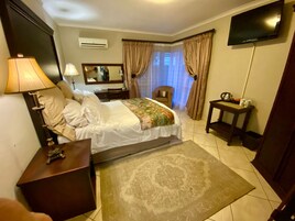 Quarto de hotel com cama, escrivaninha, cadeira, televisão e janela com cortinas.