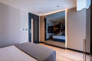 Quarto moderno com cama, espelho e televisão no quarto vizinho.