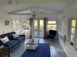 Quarto com sofá azul, poltrona azul, uma mesinha e vista para um espaço de pátio exterior através de uma porta de vidro.