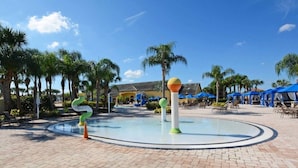 Área de piscina com um elemento aquático circular, palmeiras e espreguiçadeiras.