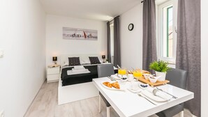 Quarto de hotel moderno com cama, mesa de cabeceira e área de jantar com preparação para o café da manhã.