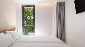 Quarto de hotel moderno com uma cama grande, janela com vista para árvores e televisão de tela plana na parede.