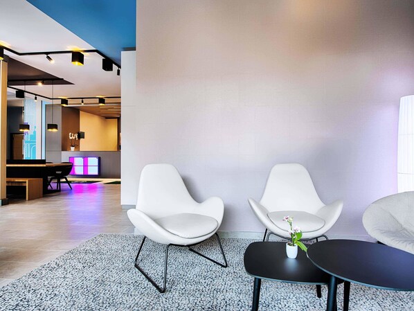 Um interior moderno com duas cadeiras brancas, uma pequena mesa preta e uma planta decorativa.