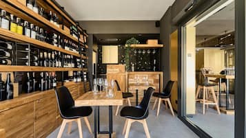 Uma área de jantar moderna com mesa de madeira, cadeiras pretas e uma adega cheia de garrafas.